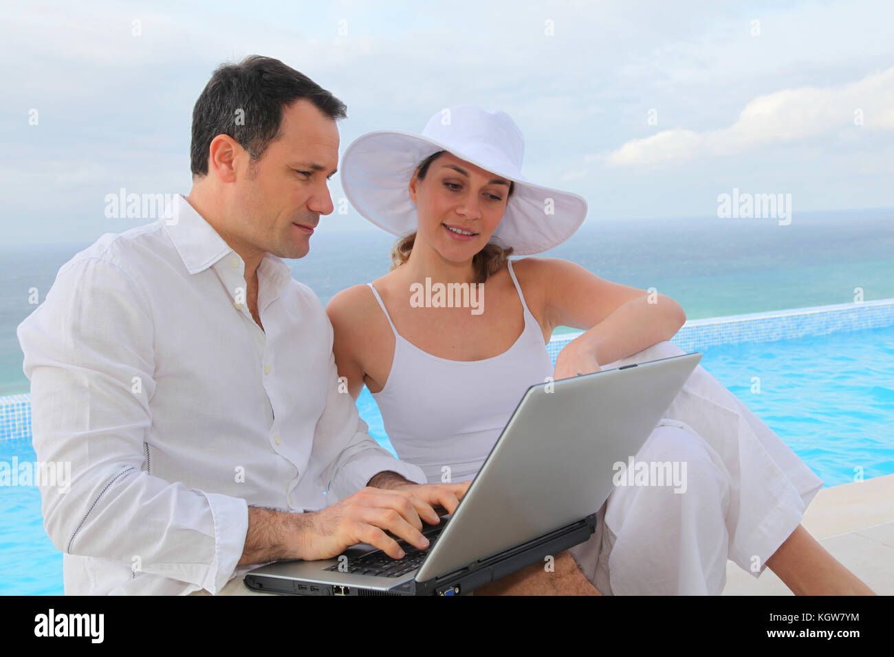 Couple using laptop computer by swimming-pool Stock Photo - Alamy