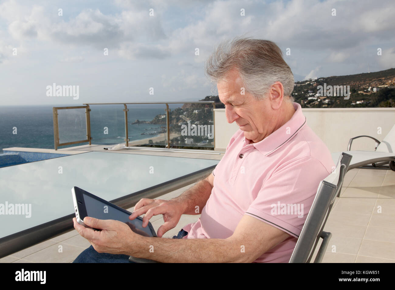 Senior man using electronic tablet by a swimming-pool Stock Photo - Alamy