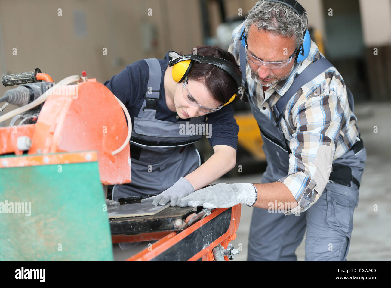 Tiler showing apprentice how to use thermal grinder Stock Photo - Alamy