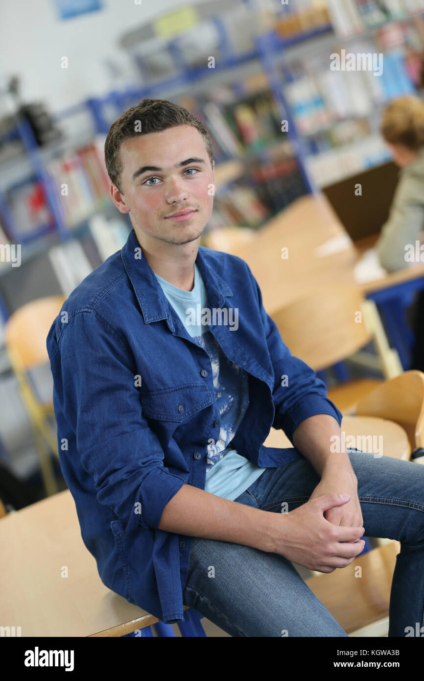 Student boy sitting on table in library room Stock Photo - Alamy