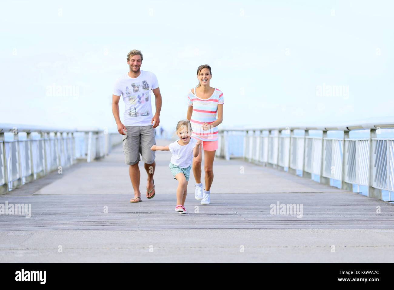 Little girl with parents running on a bridge Stock Photo - Alamy