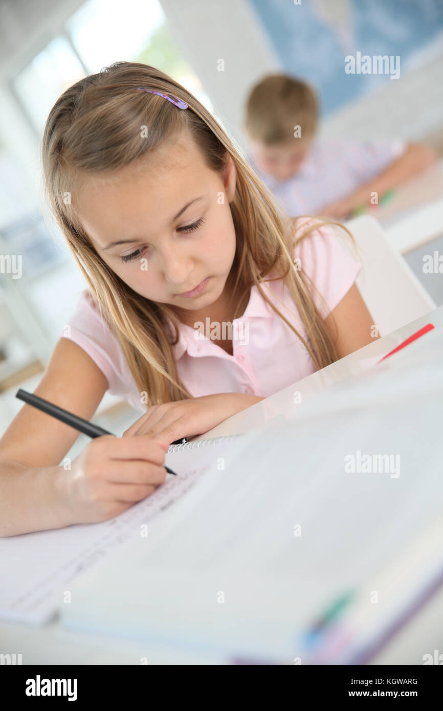 Cute schoolgirl writing on notebook, in classroom Stock Photo - Alamy