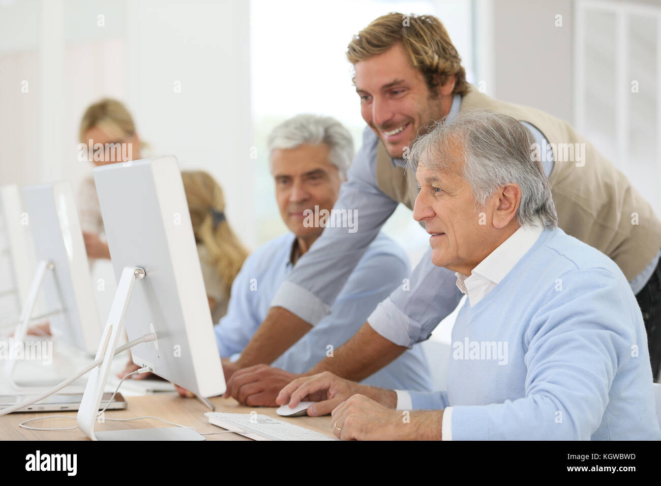 Instructor helping senior men with computing class Stock Photo - Alamy