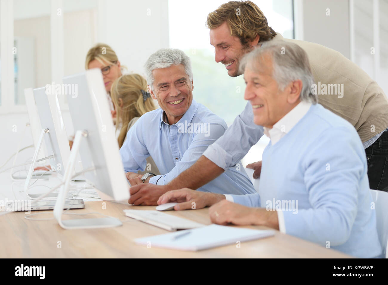 Instructor helping senior men with computing class Stock Photo - Alamy