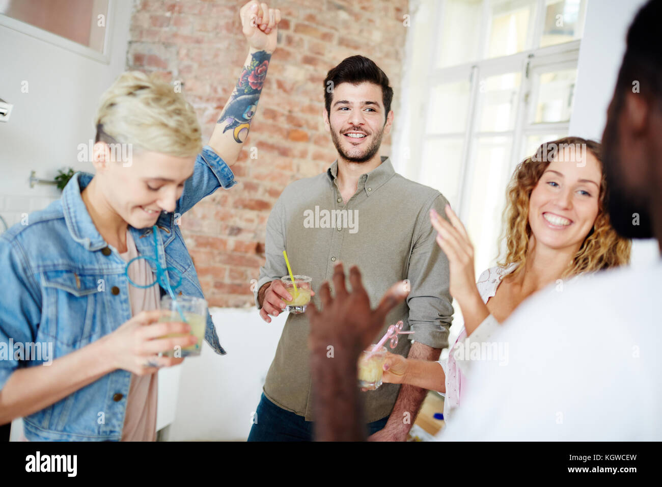 Intercultural friends with drinks dancing at home party and having talk ...