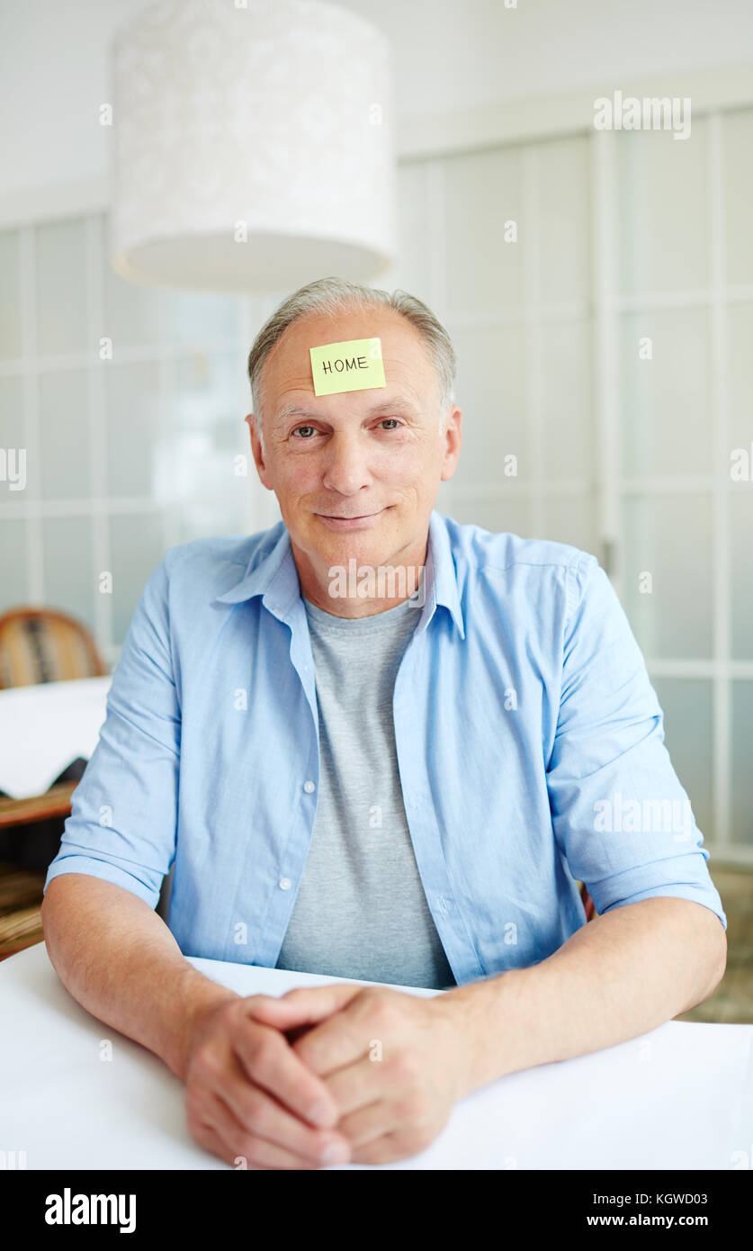 Aged man with notepaper on forehead looking at camera during leisure ...