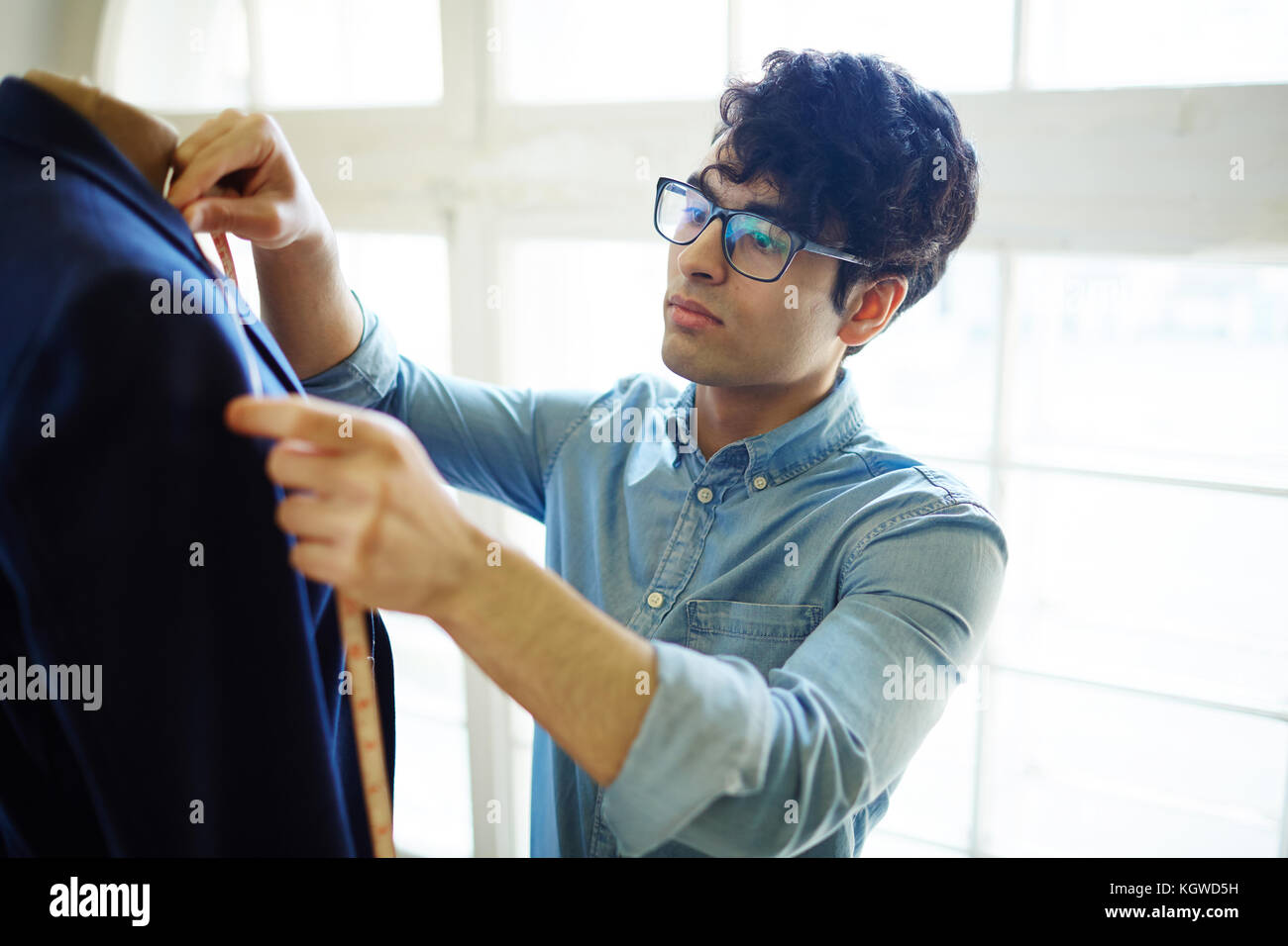 Serious tailor measuring length of jacket shoulder in his workshop ...