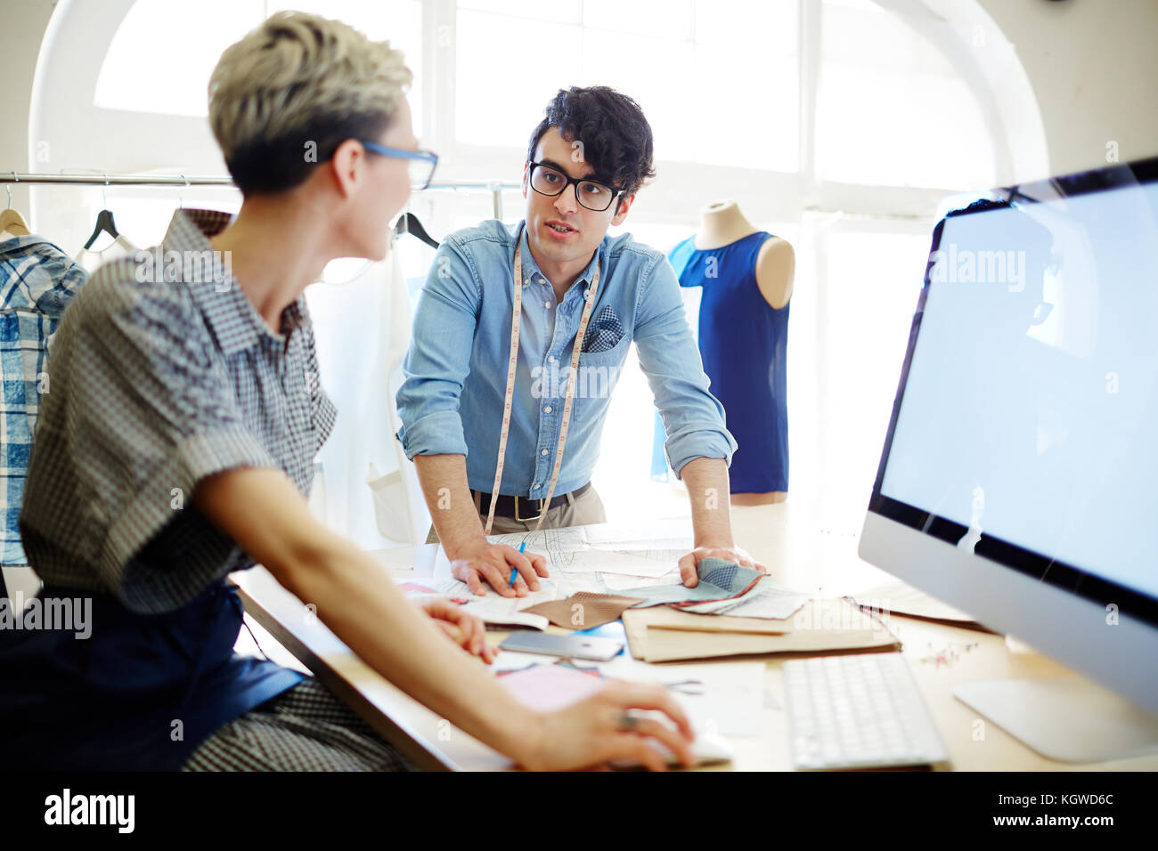 Two young fashion designers consulting about dress models and fabric ...