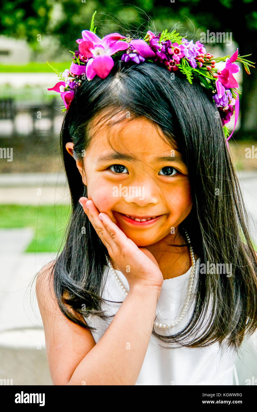 A close up view of a cute Asian flower girl smiling, a flower wreath on ...