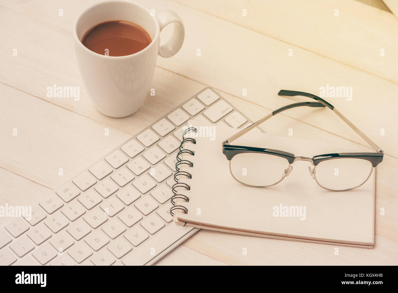 Notepad and computer keyboard on white table with eyeglasses, coffee ...