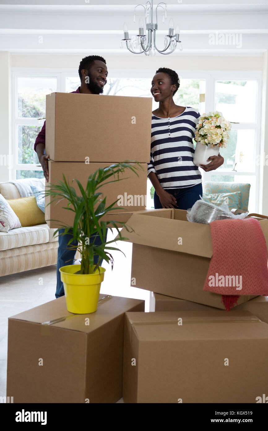 Happy Couple Carrying Big Cardboard Box And Vase At New Home Stock