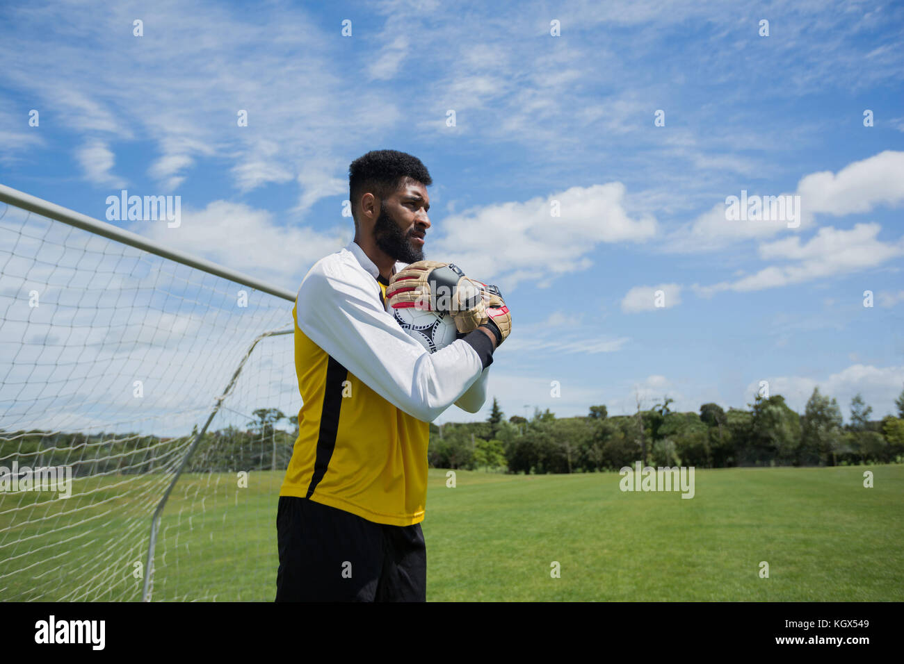 Goalkeeper holding football in front of goal post on a sunny day Stock ...