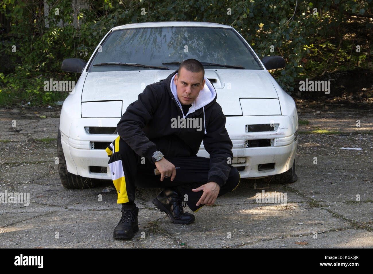 A young man, gopnik kneeling next to an abandoned car Stock Photo - Alamy