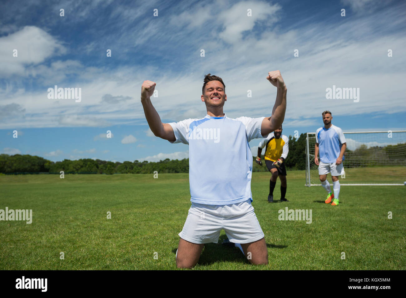 Excited football player in celebrating scoring goal kneeling on grass ...