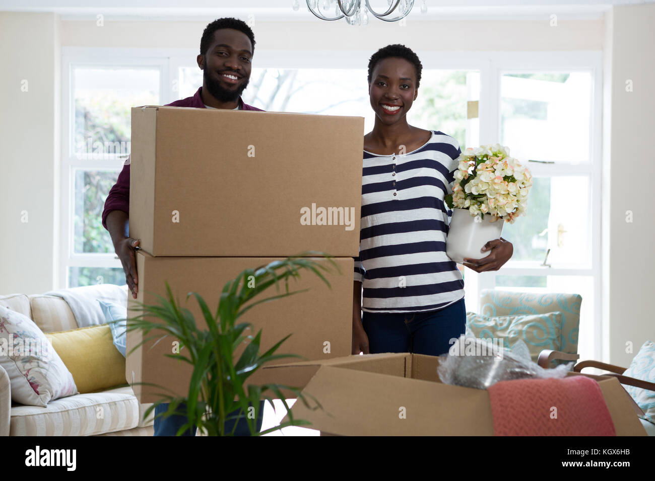 Portrait of couple carrying big cardboard box and vase at new home ...