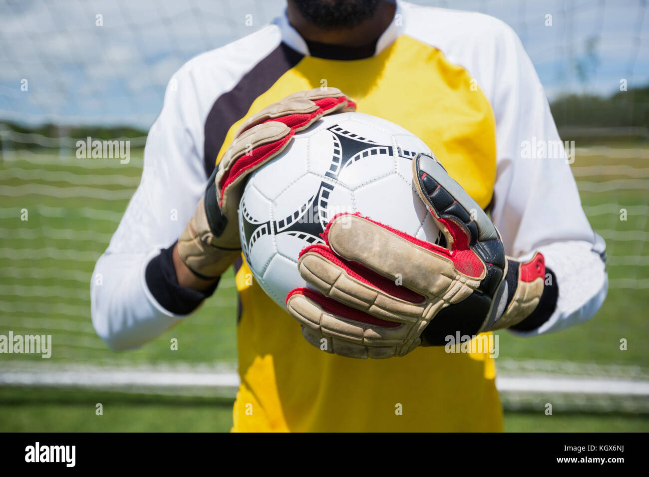 Mid section of goalkeeper with ball standing in front of goal post ...