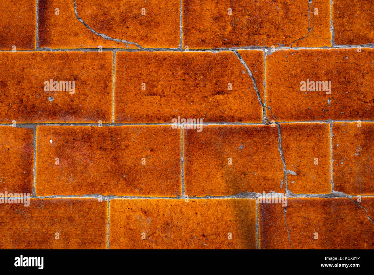 Detail of old wall of ceramic orange chipped bricks with several cracks ...