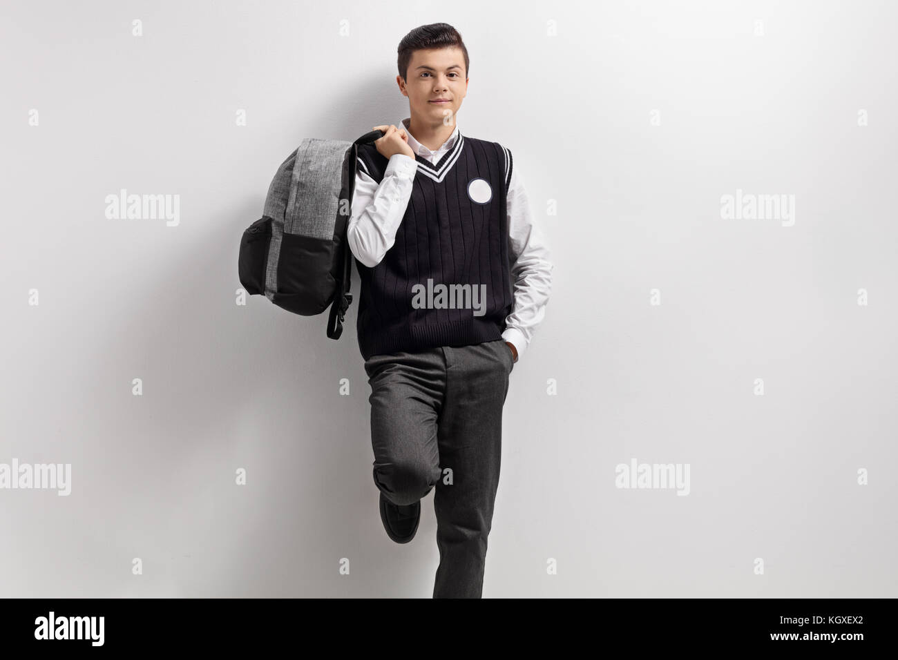 Teenage student holding a backpack and leaning against a wall Stock ...