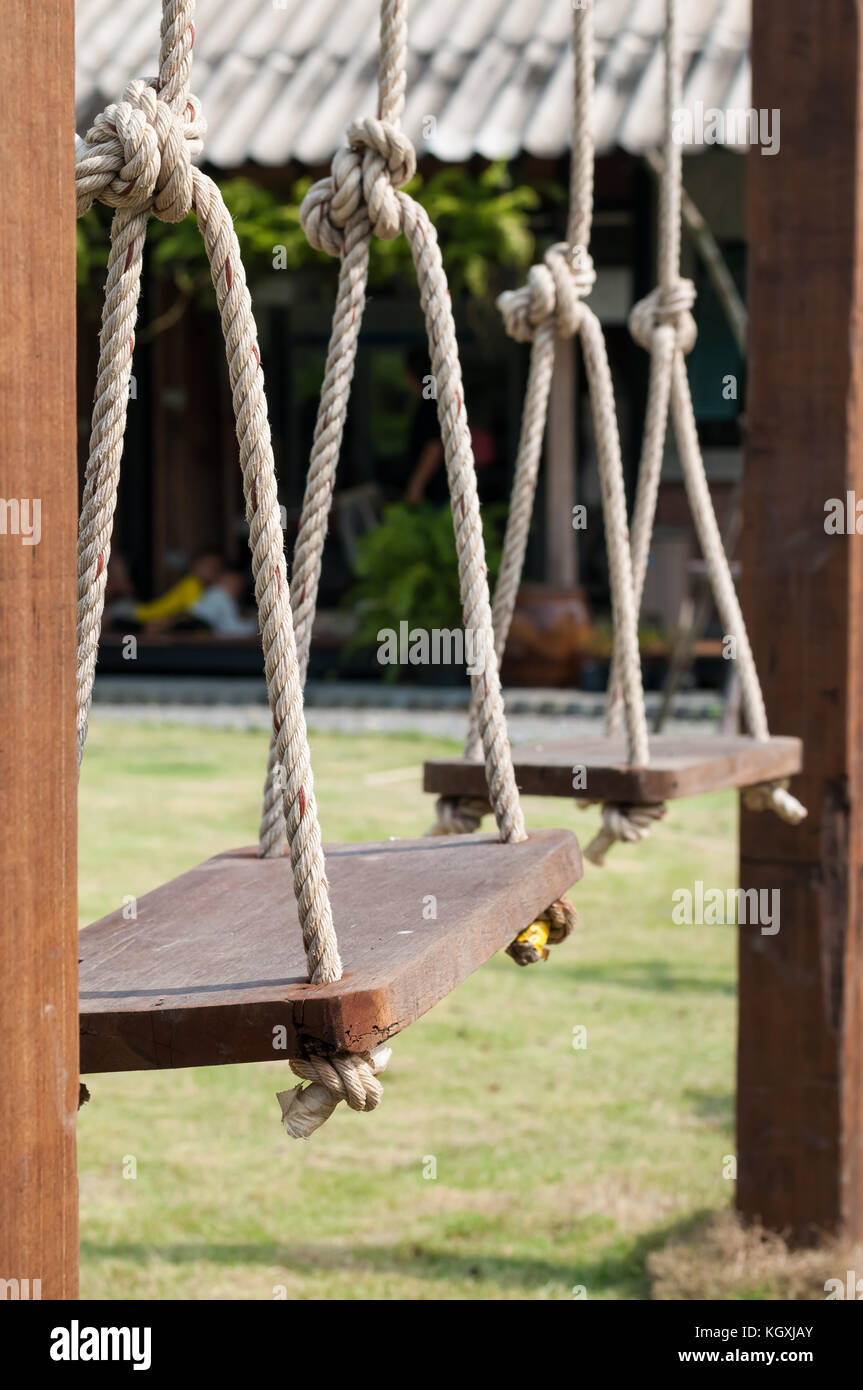Selected focus wooden swing hung by ropes in green lawn playground ...