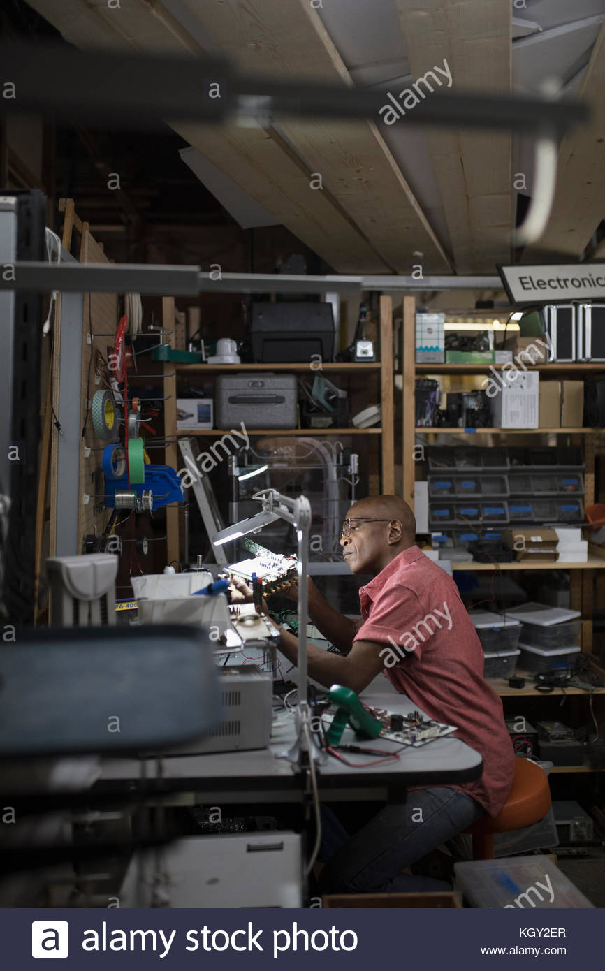 Senior male engineer examining electronics under lamp at workbench in ...