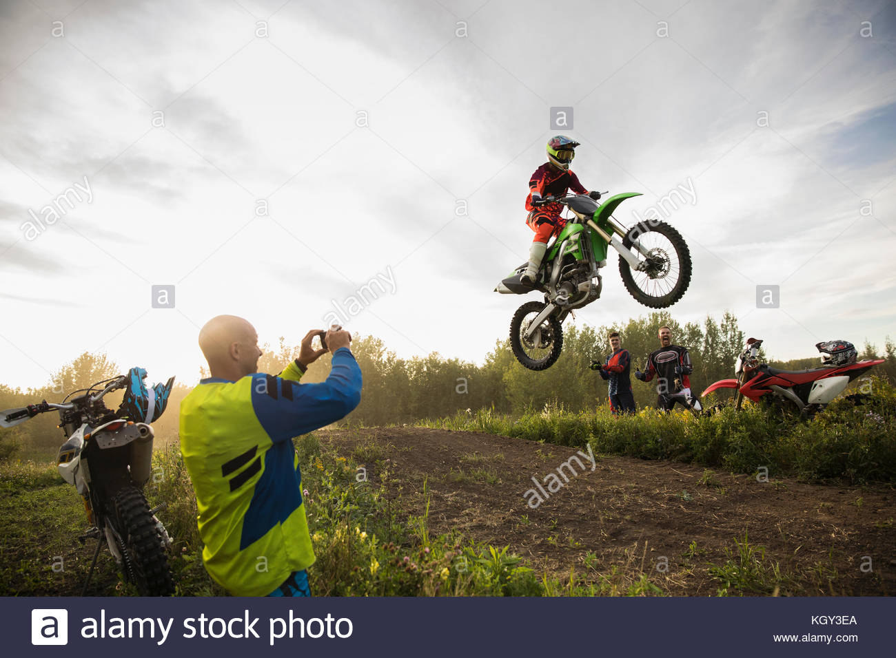 Man with camera phone photographing friend doing motorbike stunt jump ...