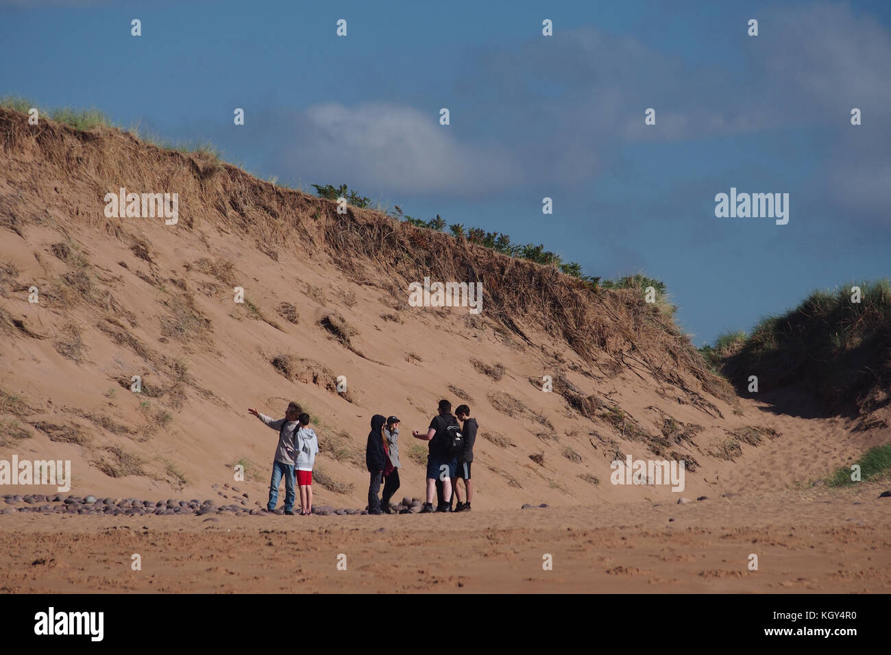 Group of friends standing by the sand dunes on the beach at Red Point ...