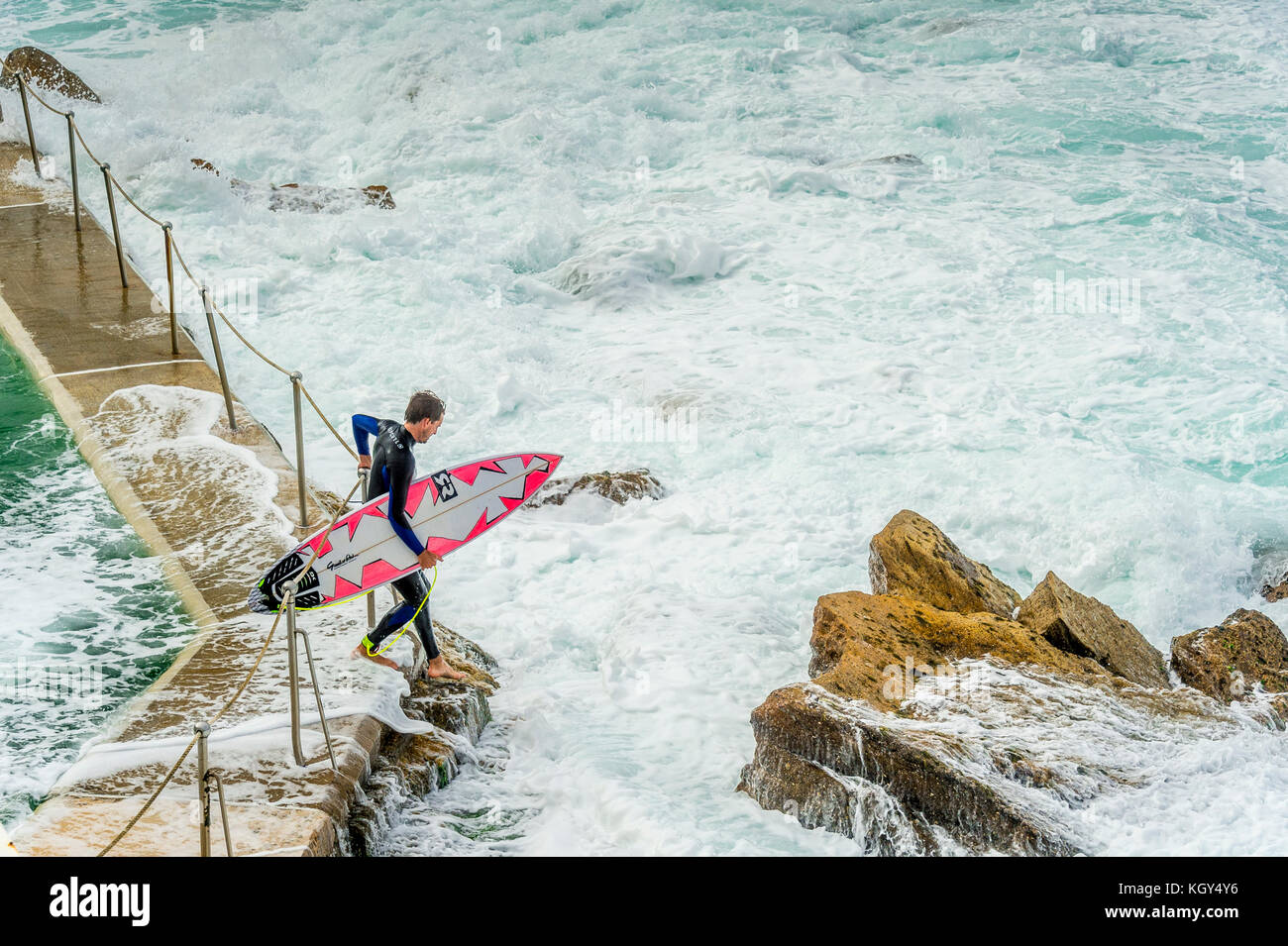 A surfer carefully steps onto rocks and into dangerous surf conditions ...