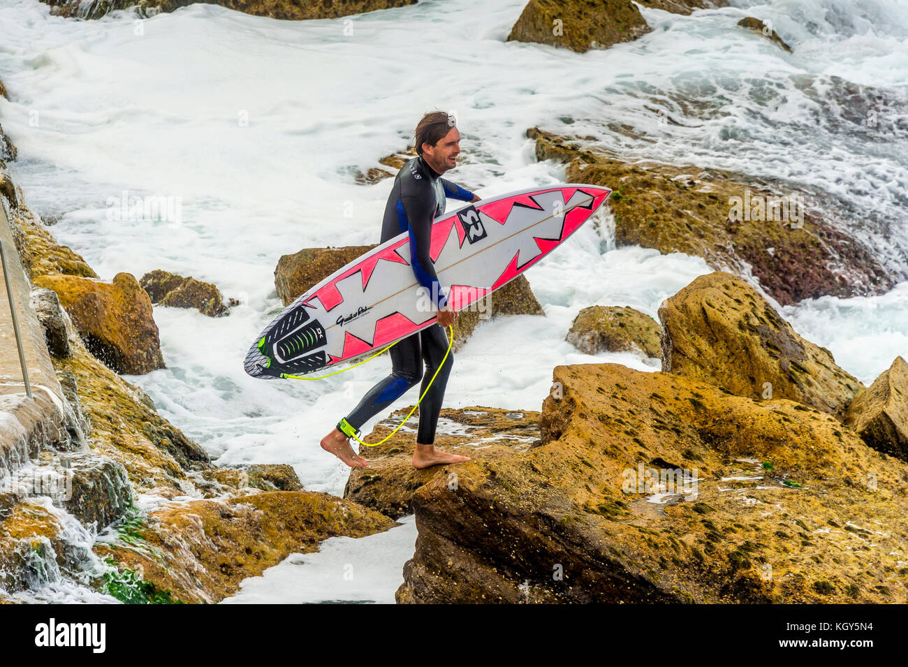 A surfer carefully steps onto rocks and into dangerous surf conditions ...