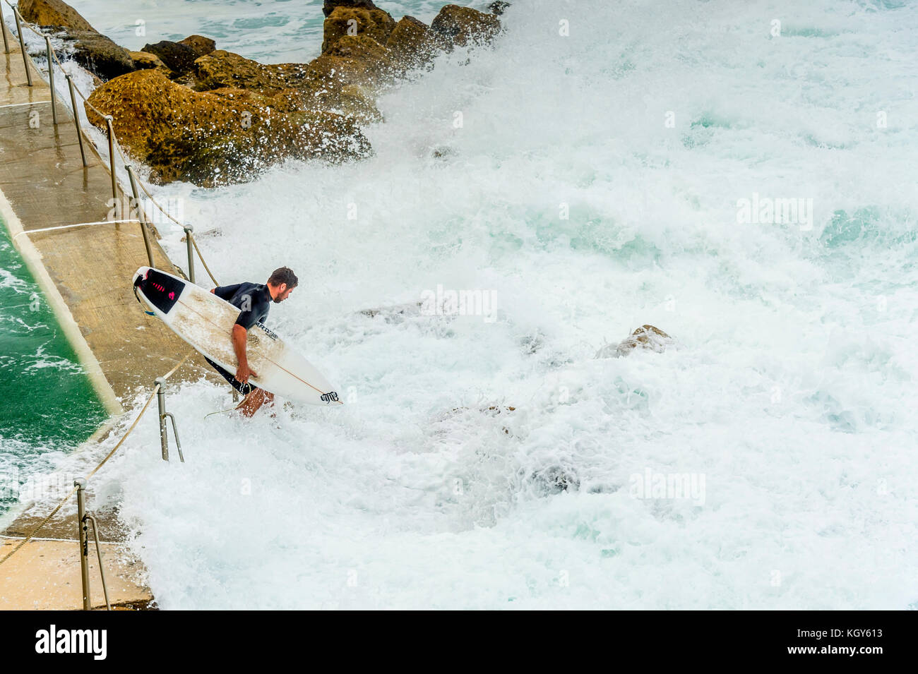 A surfer carefully steps onto rocks and into dangerous surf conditions ...