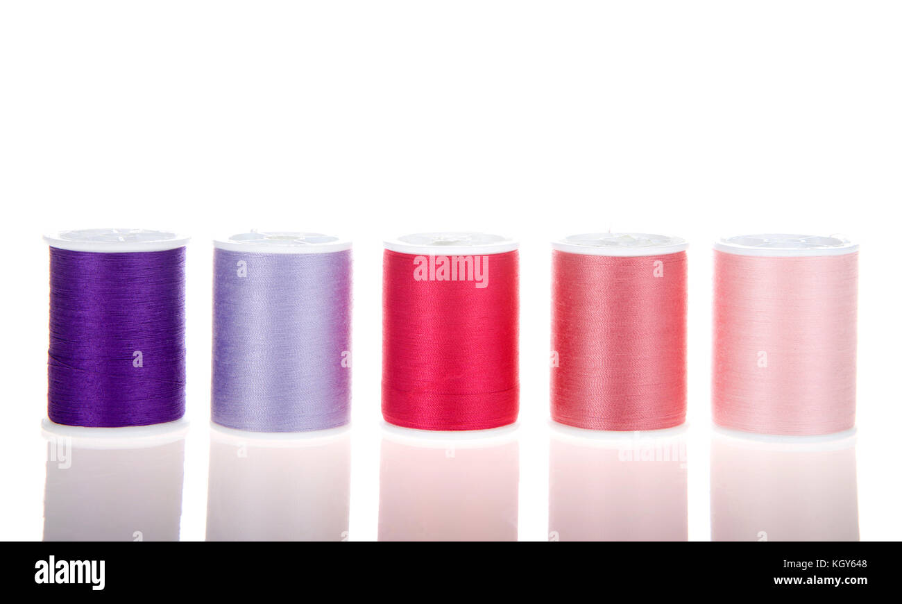 Five spools of thread isolated on white sitting on a reflective surface ...