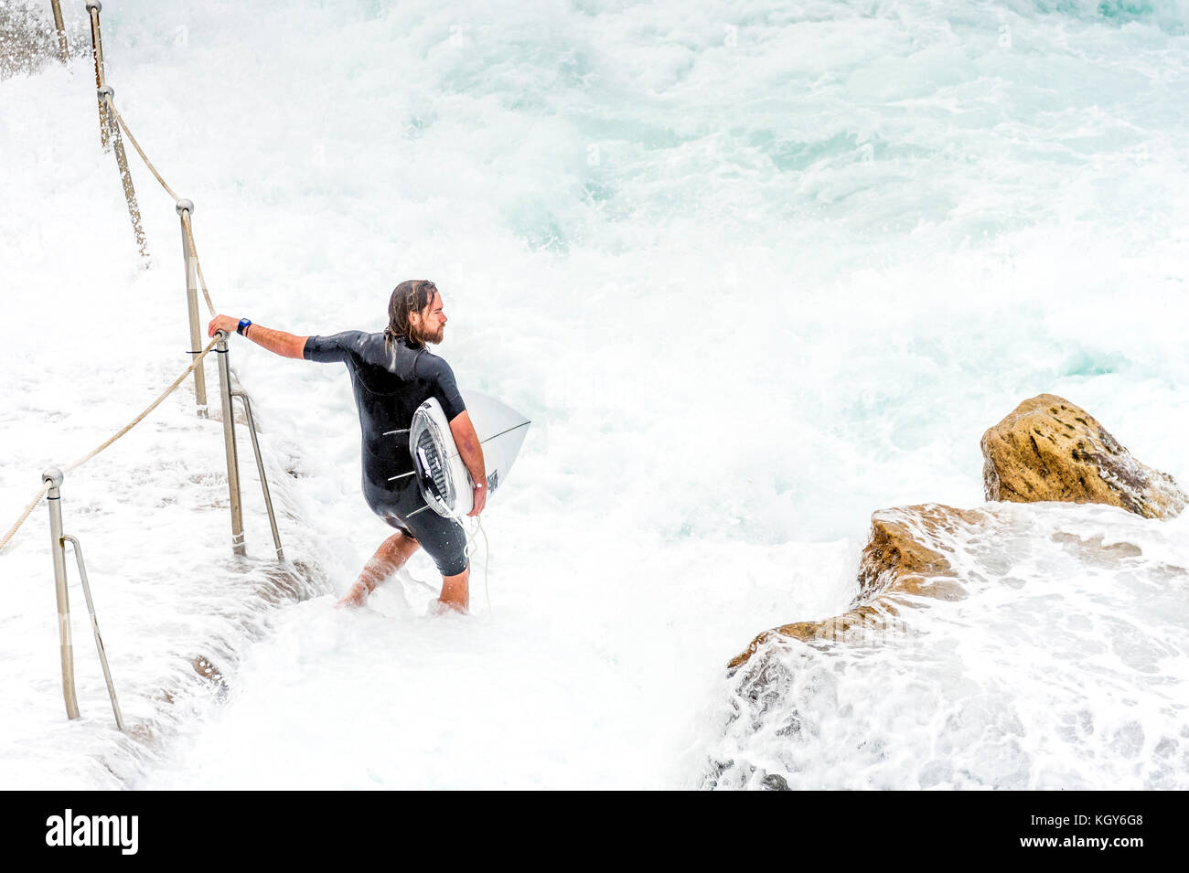 A surfer carefully steps onto rocks and into dangerous surf conditions ...