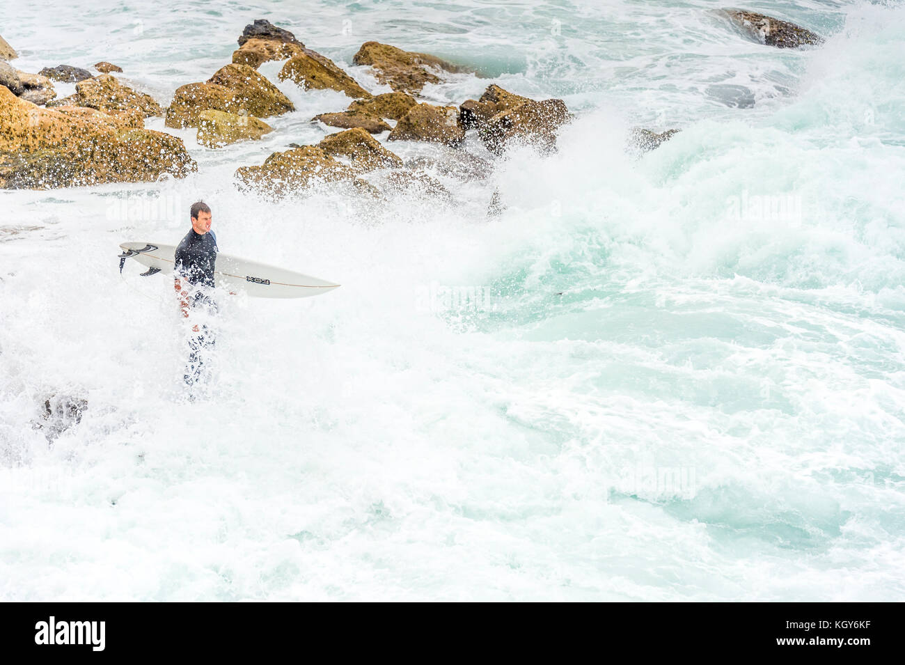 A surfer carefully steps onto rocks and into dangerous surf conditions ...
