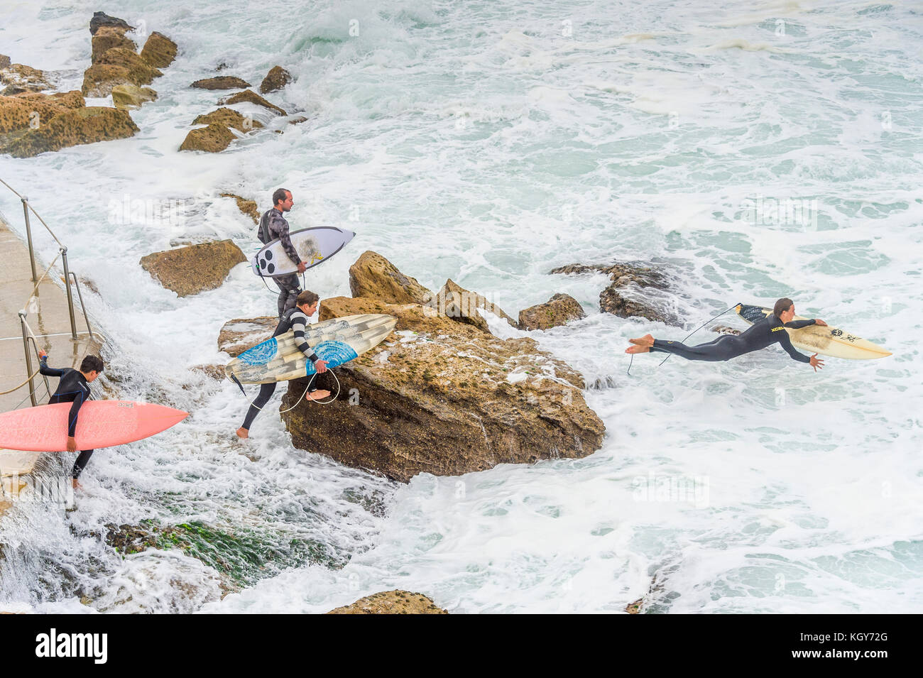 Surfers carefully step onto rocks and into dangerous surf conditions at ...