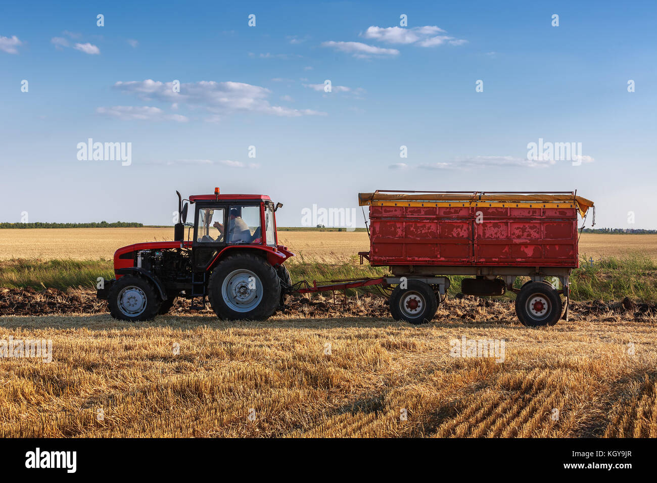 Red tractor with red trailer ina field Stock Photo - Alamy