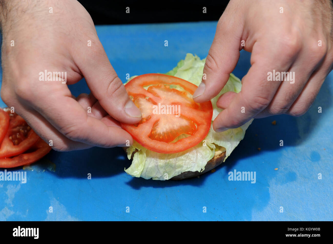 Cook adding tomato on burger in the kitchen. Preparing and making ...