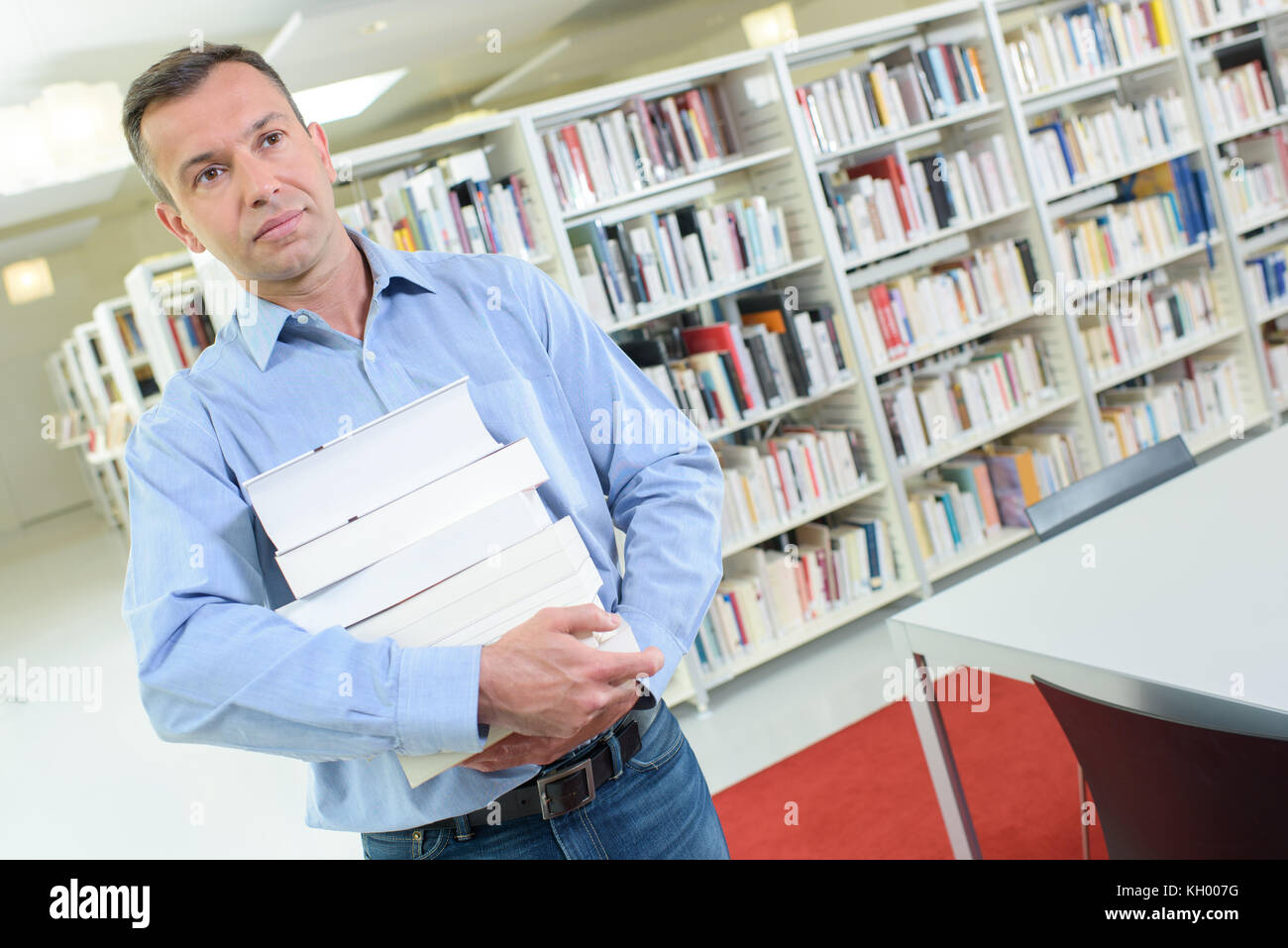 Man carrying stack of books in library Stock Photo - Alamy