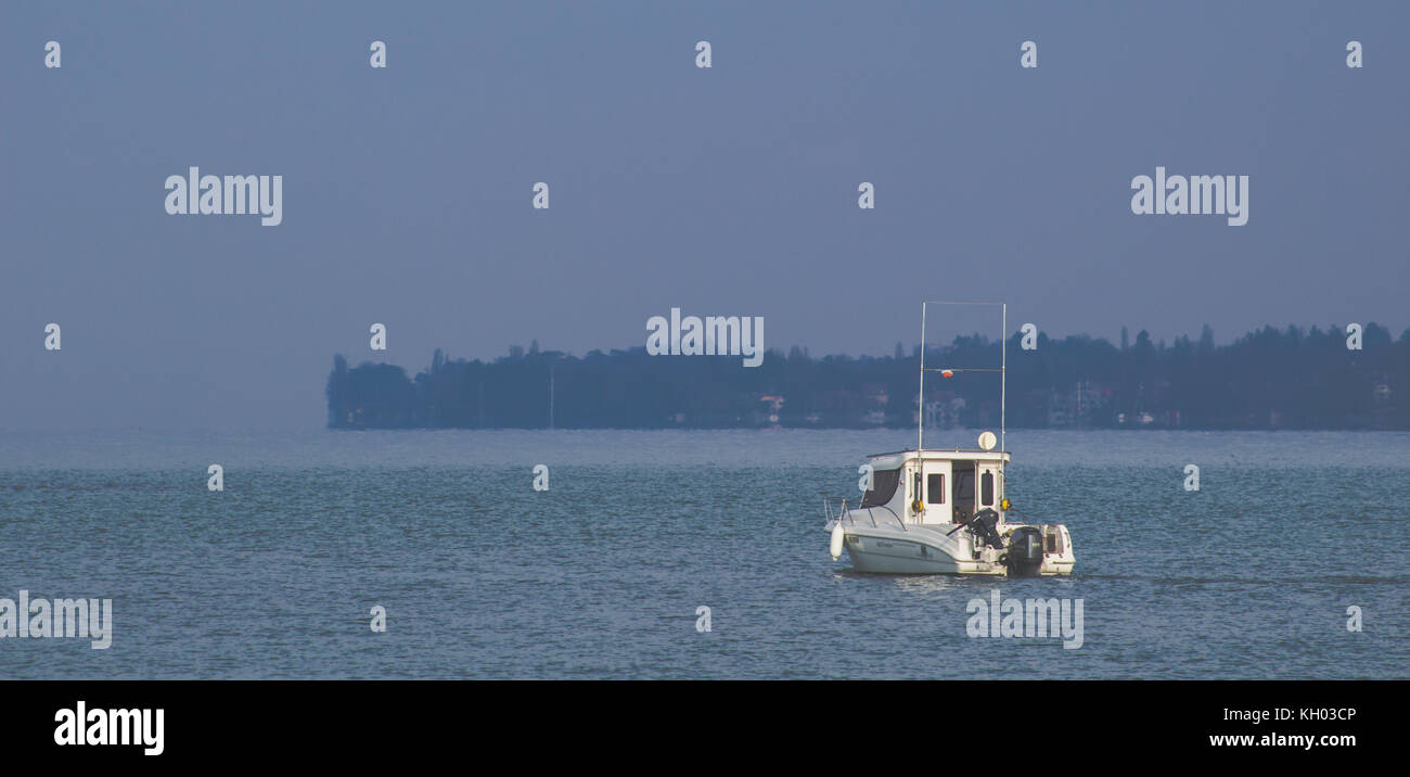 boat sailing away on lake with trees in the background Stock Photo - Alamy