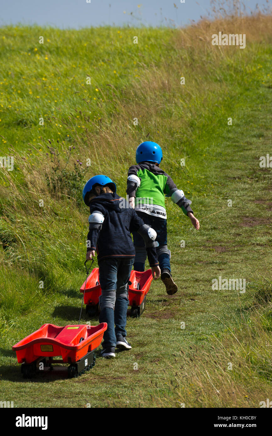 Two boys pulling grass sledges up a slope Stock Photo - Alamy