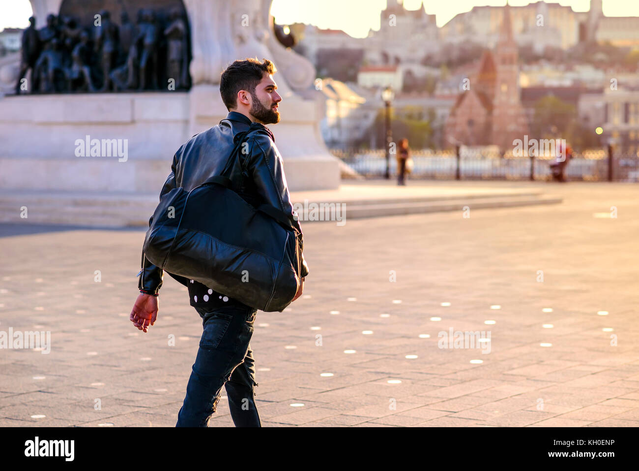 A handsome young hipster man walking and looking around on a square in ...