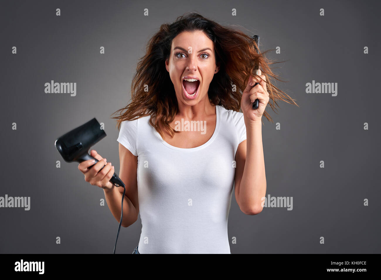 A beautiful young woman screaming while using a hairdryer and a ...