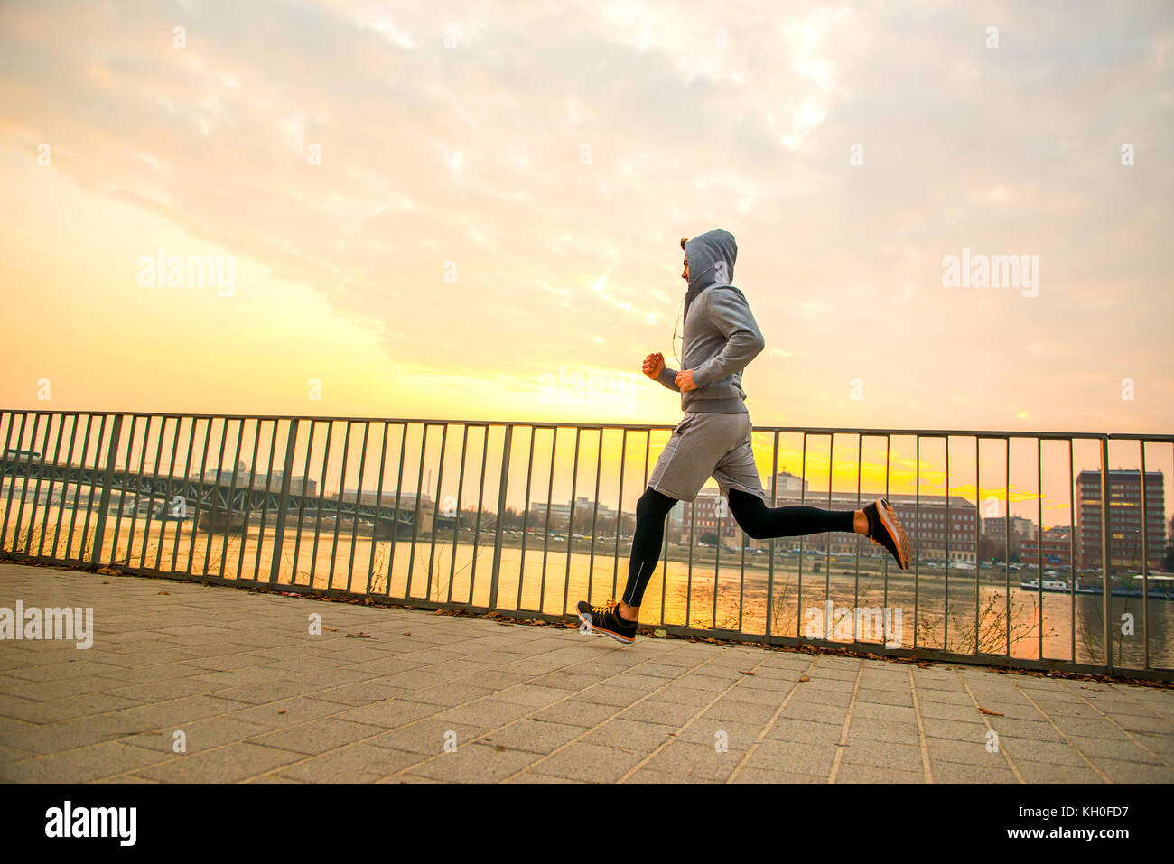 A handsome young man running in the sunset next to a fence on the ...