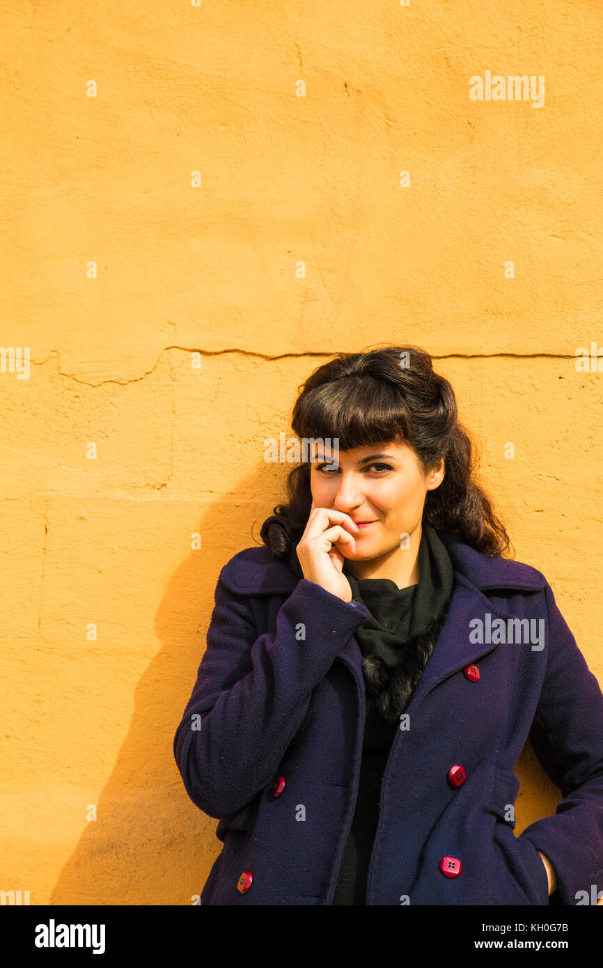 A smiling retro styled girl waiting and leaning against a wall Stock ...