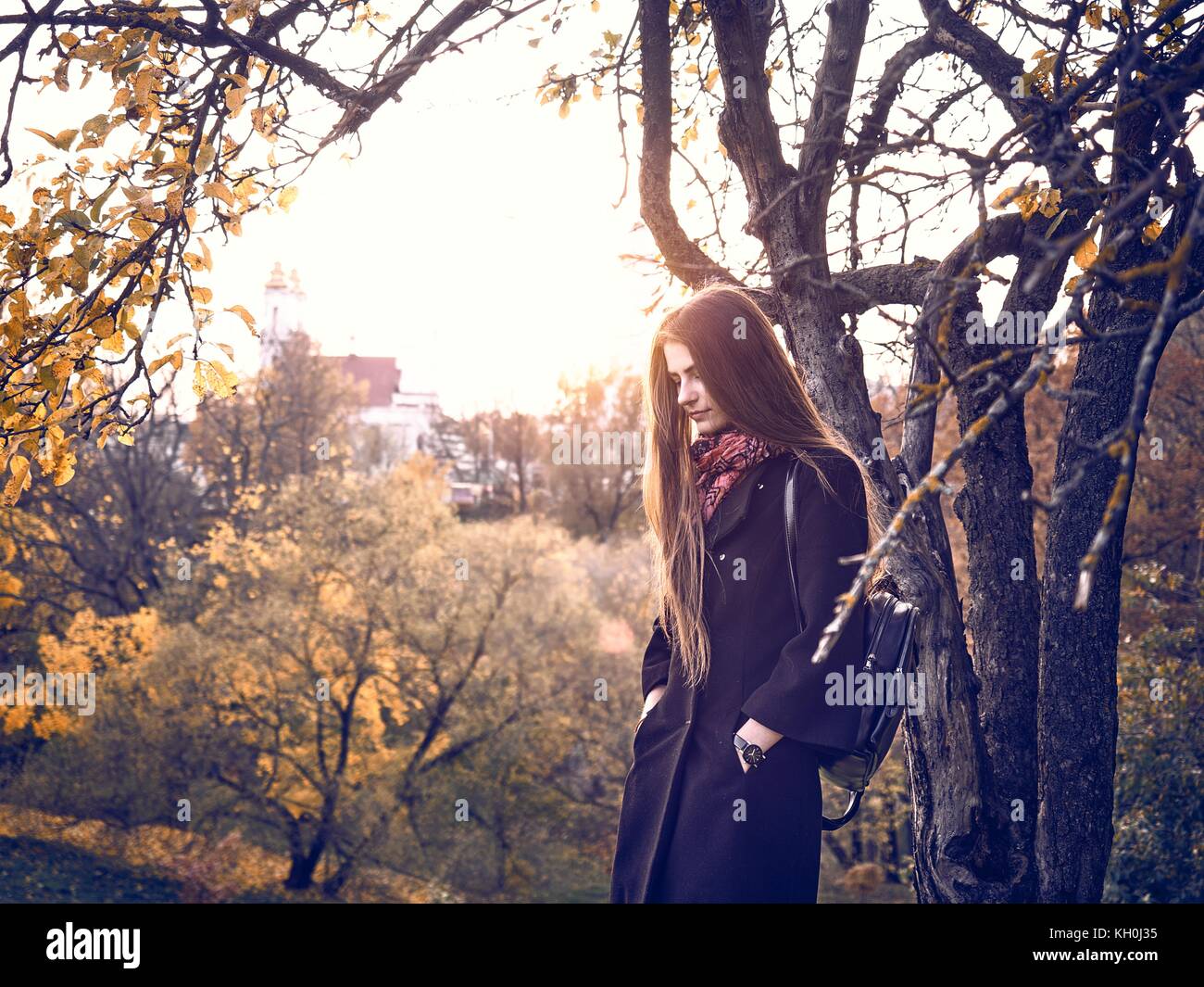 A young girl stands leaning against the trunk of an apple tree. Around ...