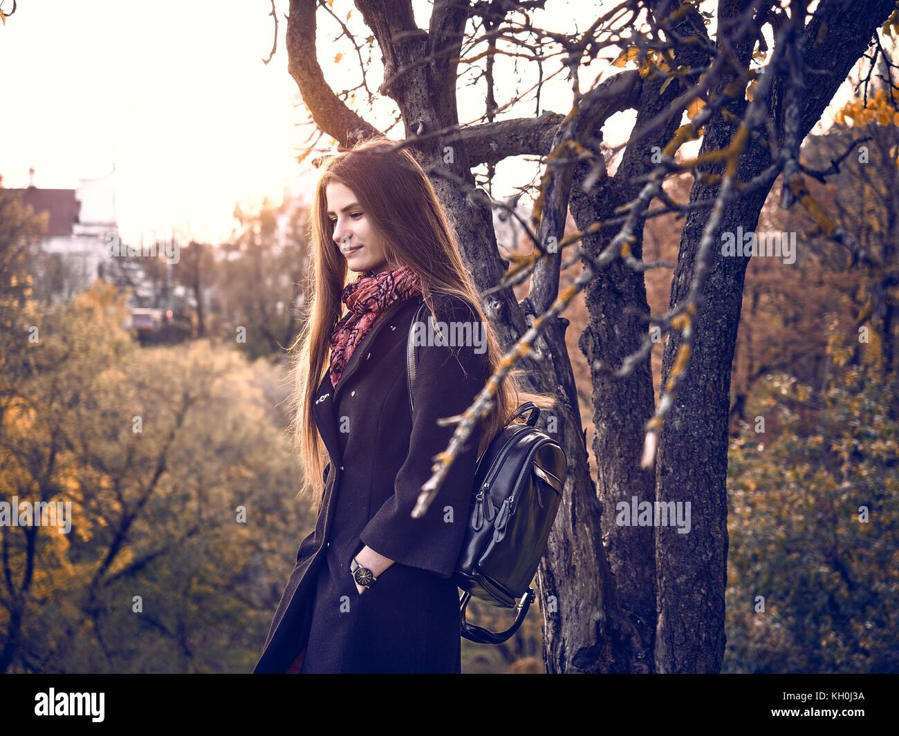 A young girl stands leaning against the trunk of an apple tree. Around ...