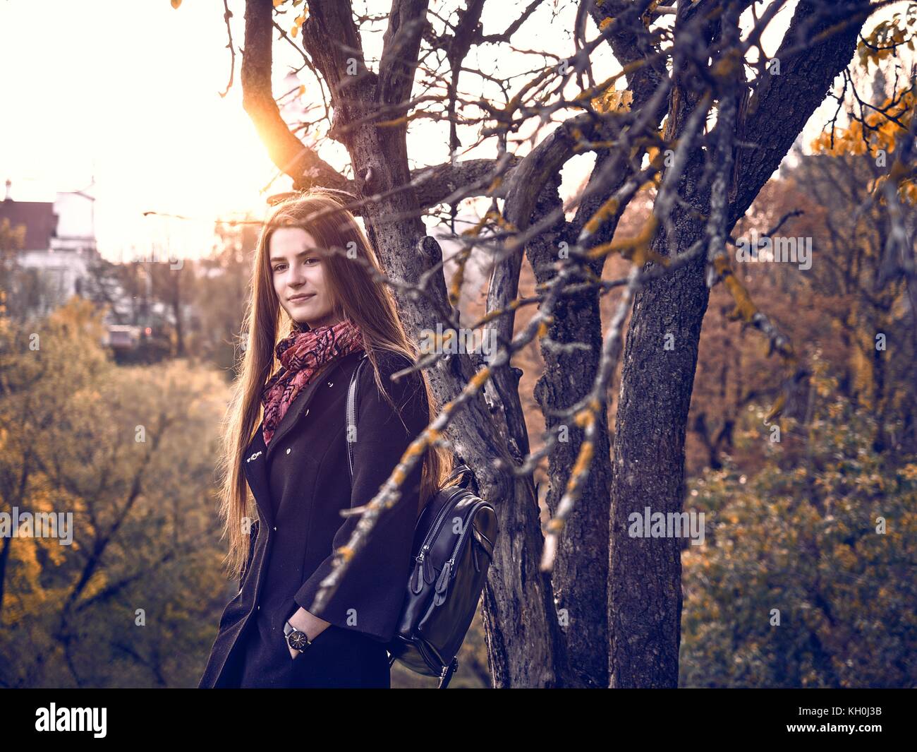 A young girl stands leaning against the trunk of an apple tree. Around ...
