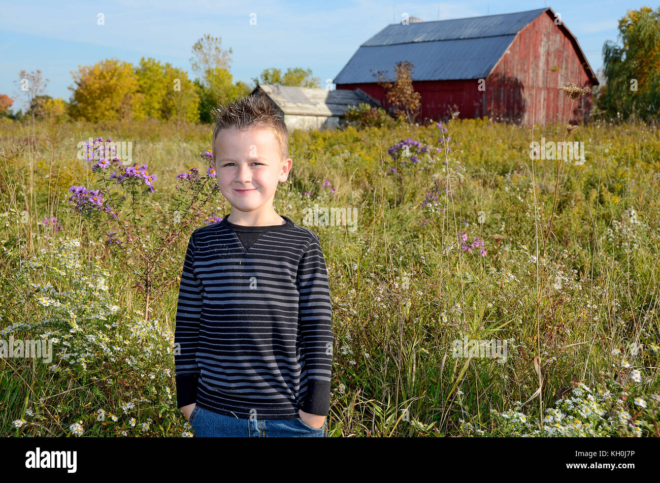 smiling Caucasian boy in wildflower field with old barn in background ...