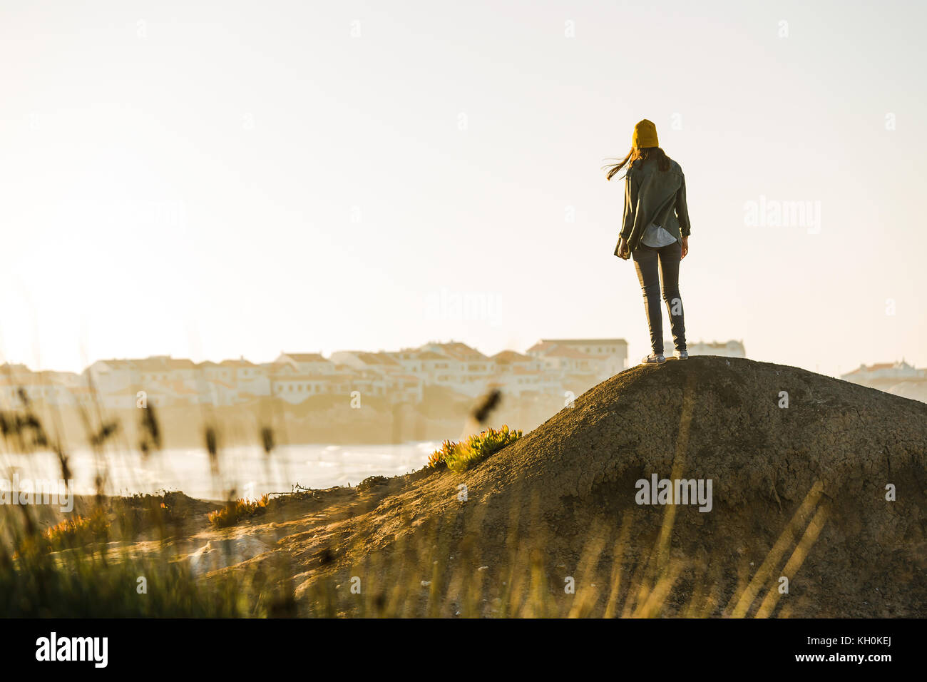 Woman with yellow cap over the cliff seeing the beach Stock Photo - Alamy