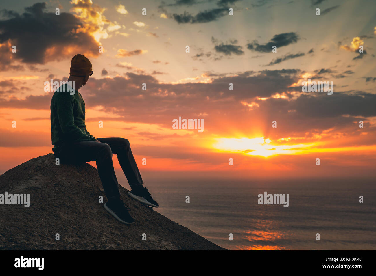Young man sitting and watching a beautiful sunset Stock Photo - Alamy