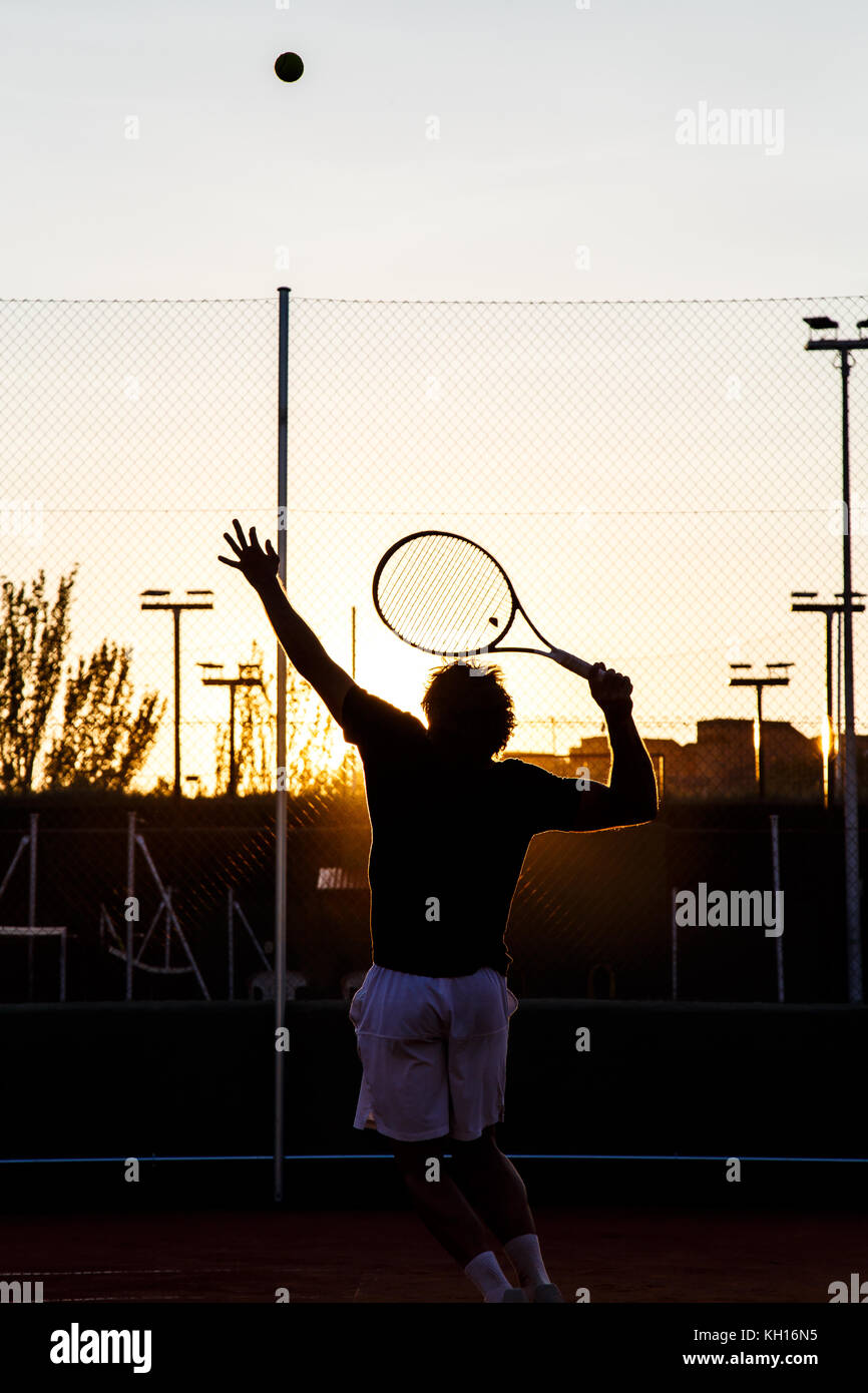 Back view of sportsman with tennis rocket hitting ball in back light on ...