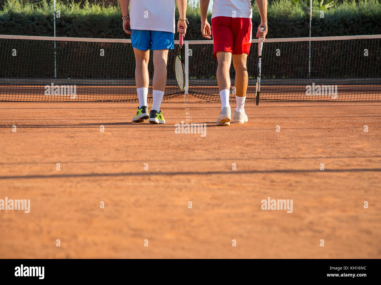 Two professional tennis players with rackets walking towards tennis net ...